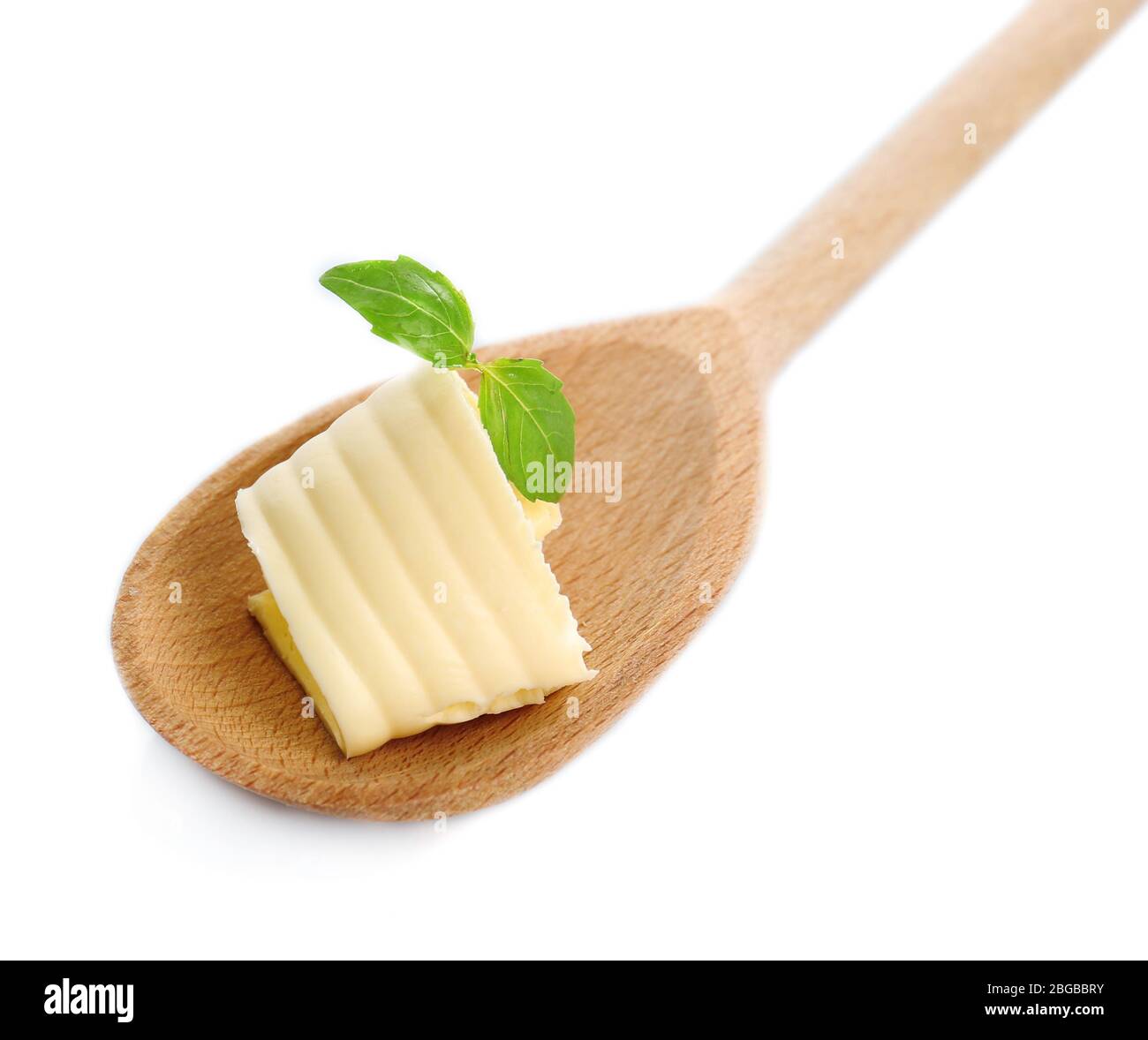 Curl of fresh butter with basil on wooden spoon, isolated on white ...