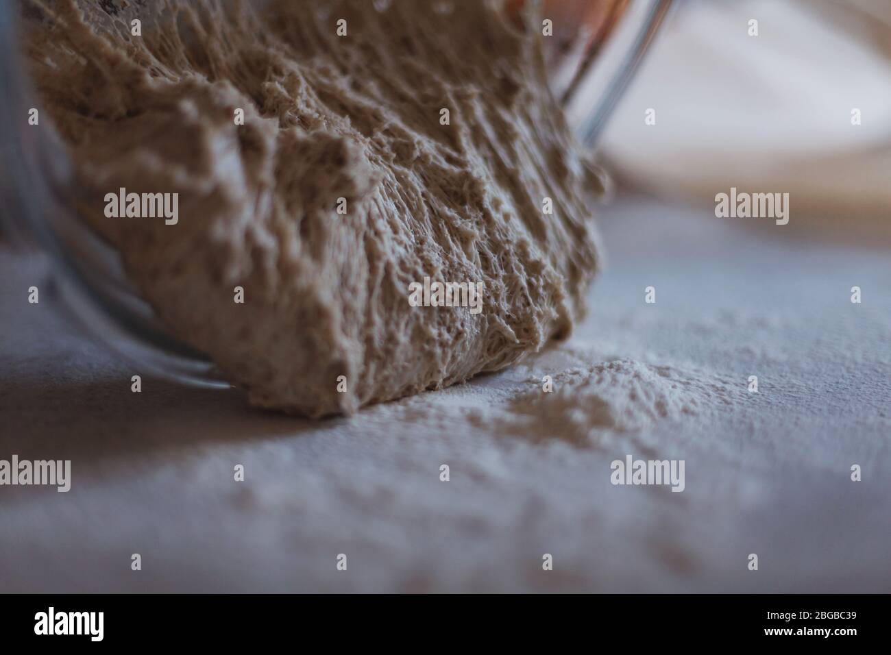 Close up of dough falling out of bowl onto table surface covered with ...