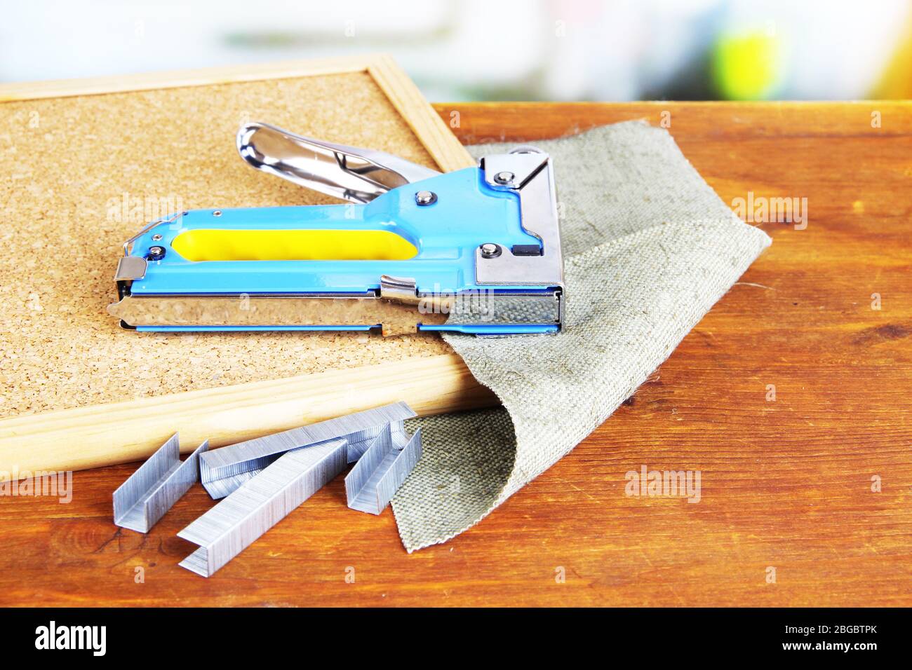 Construction stapler with staples and cork board on table on bright ...
