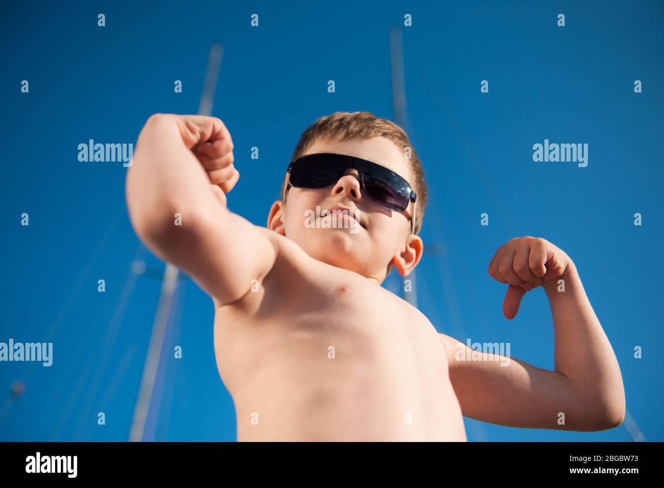 strong small kid in sunglasses demonstrates his big muscle outdoor ...