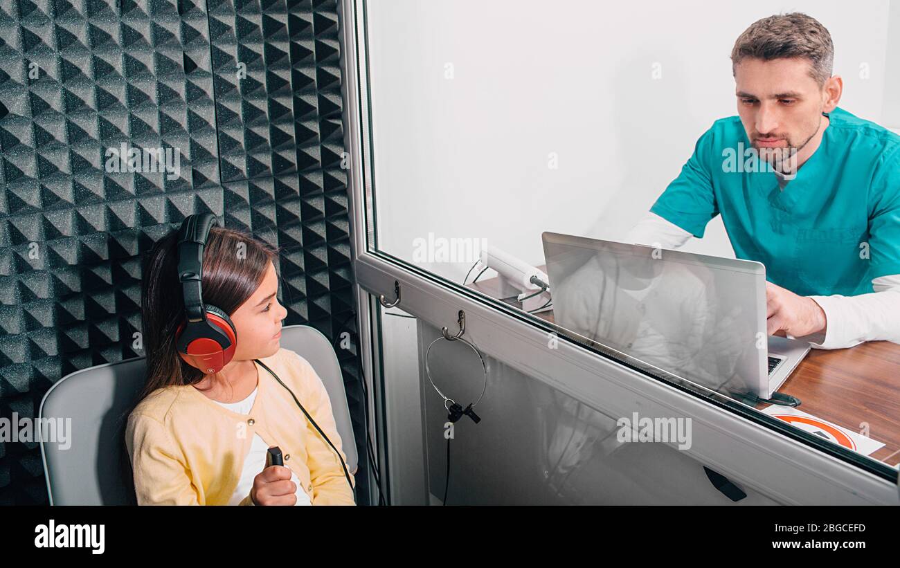 Audiologist doing a hearing test of the child. Girl complaining of bad ...