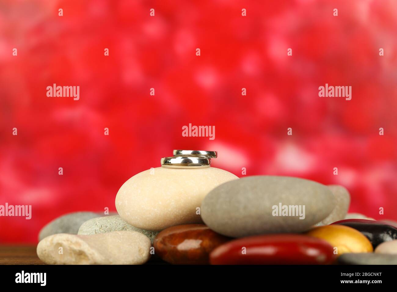 Wedding rings on rocks on red background Stock Photo - Alamy