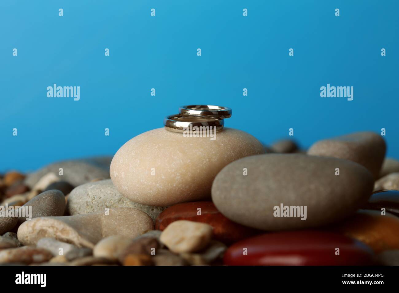 Wedding rings on rocks on blue background Stock Photo - Alamy