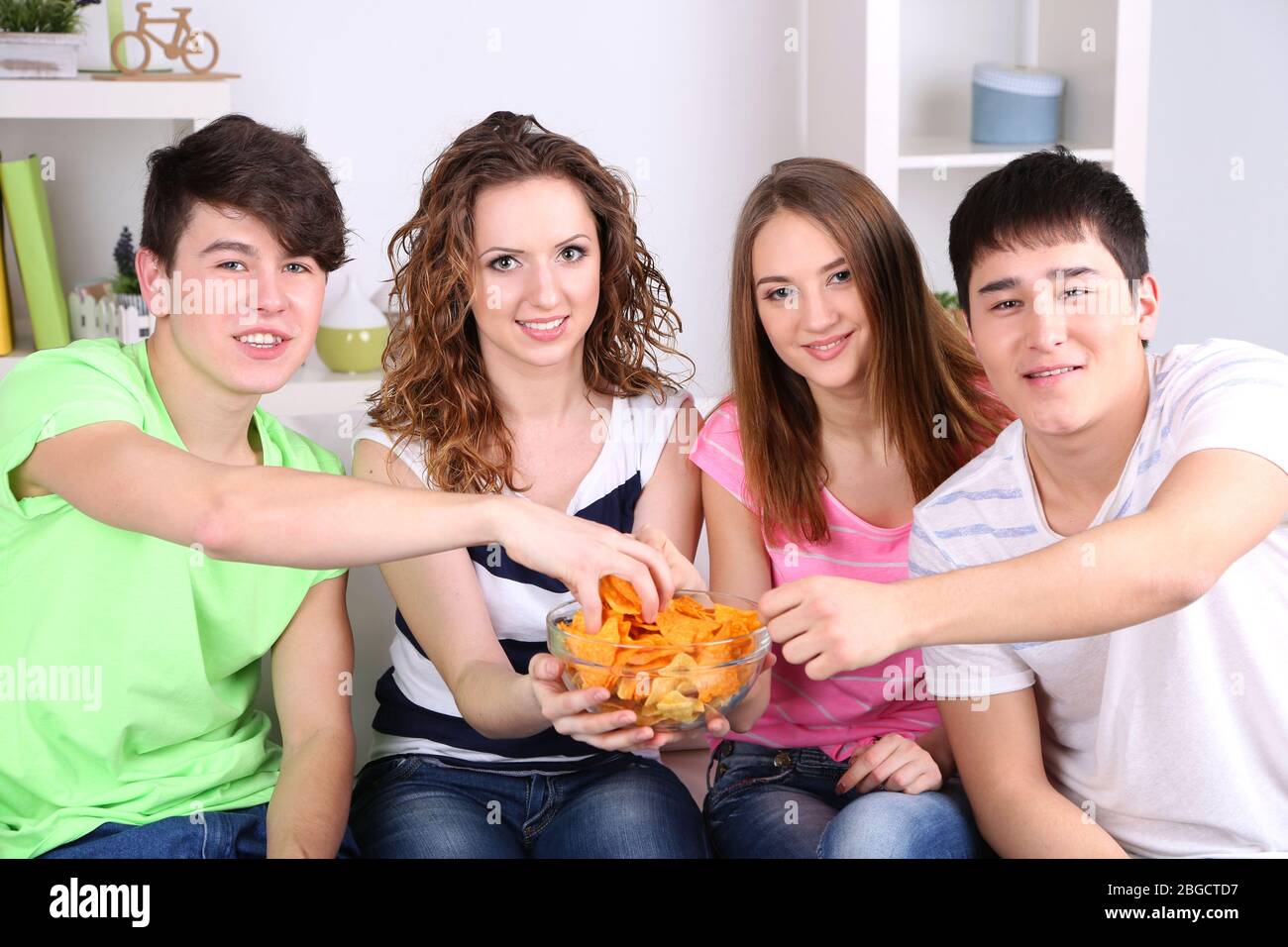 Group of young friends eating chips in living-room on sofa Stock Photo ...