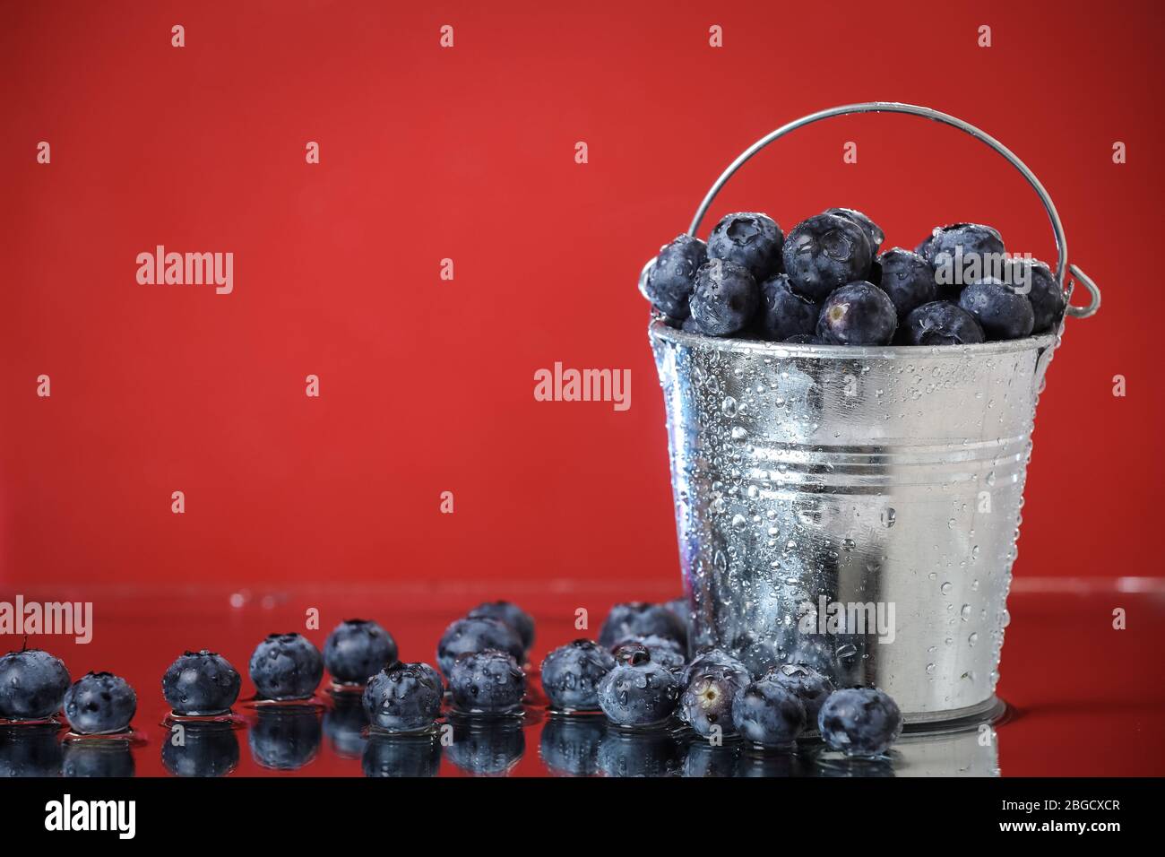 Blueberries in a metal bucket closeup on a red background. Multivitamin ...