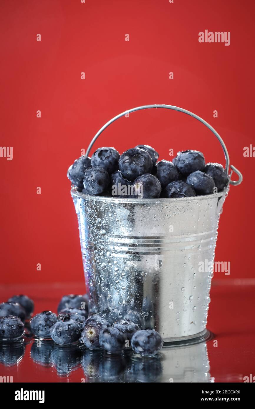Blueberries in a metal bucket closeup on a red background. Multivitamin ...