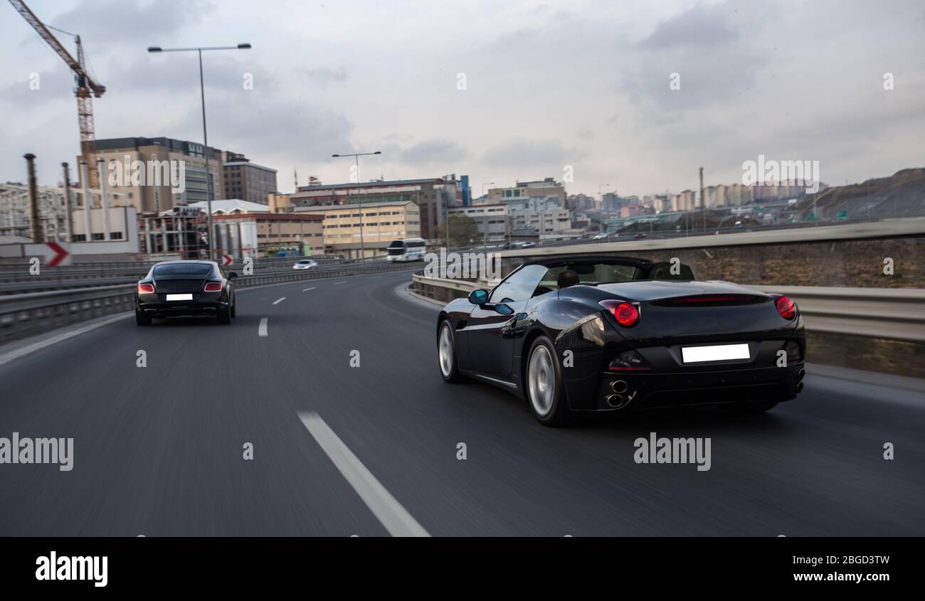 Two black cars motorshow racing on the highway in the evening time ...