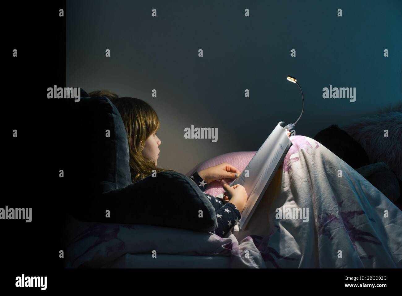 Girl reading a book in bed at night in comfy bedroom wearing pyjamas ...