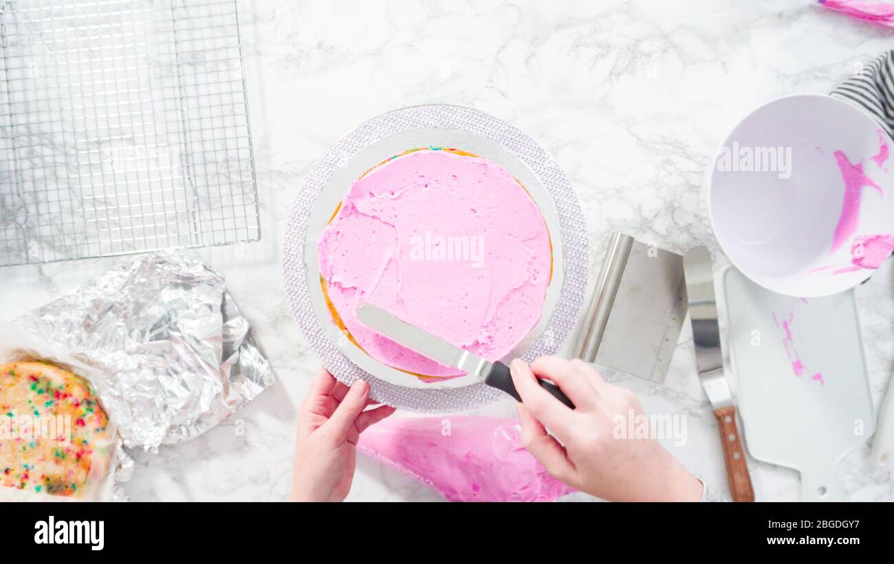 Flat lay. Step by step. Frosting round funfetti cake layers with pink ...