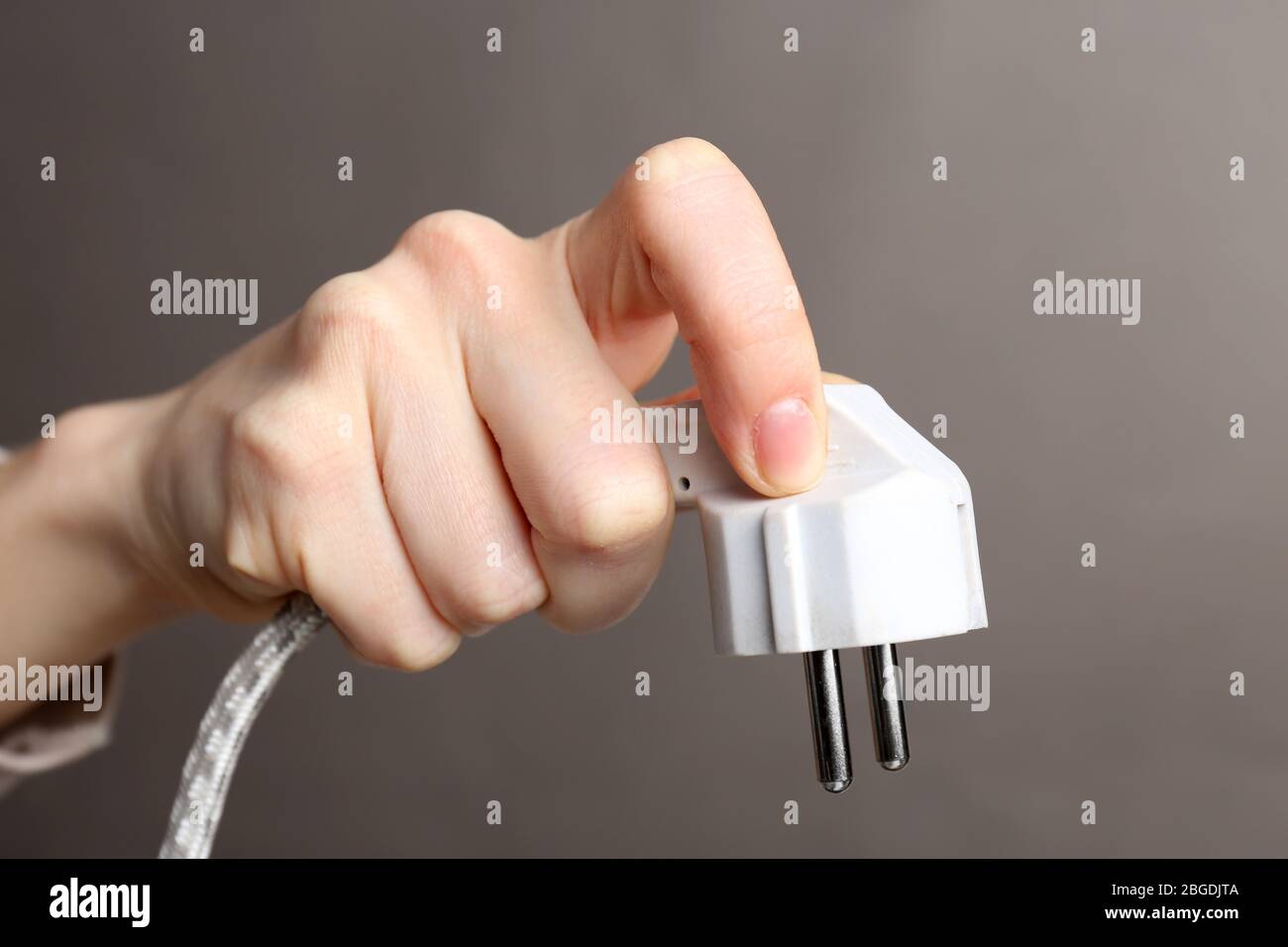 Hand holding electric plug on grey background Stock Photo - Alamy