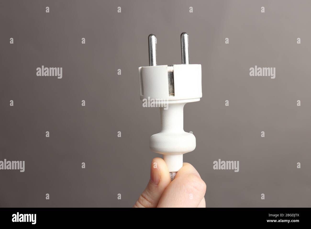 Hand holding electric plug on grey background Stock Photo - Alamy