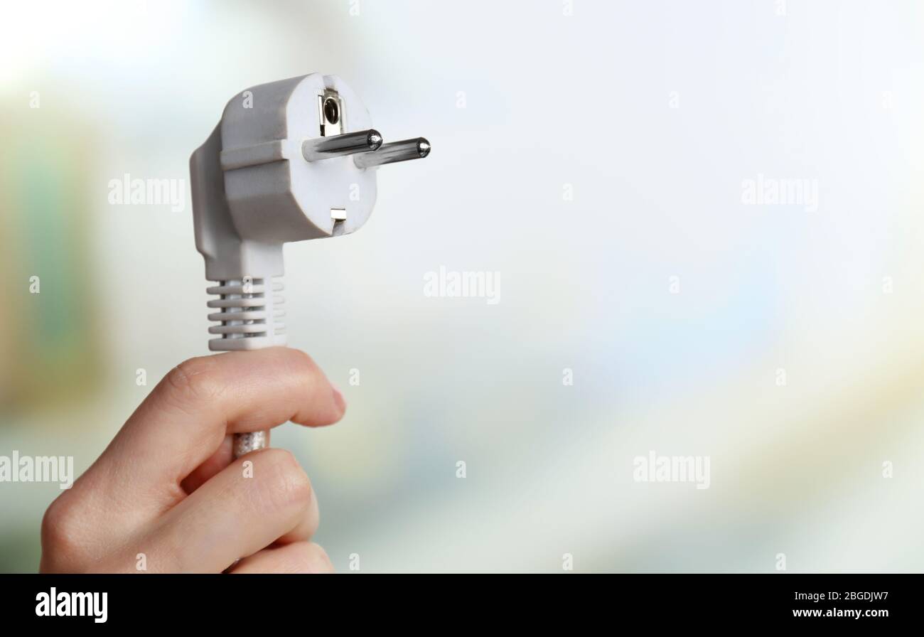 Hand holding electric plug on light background Stock Photo - Alamy