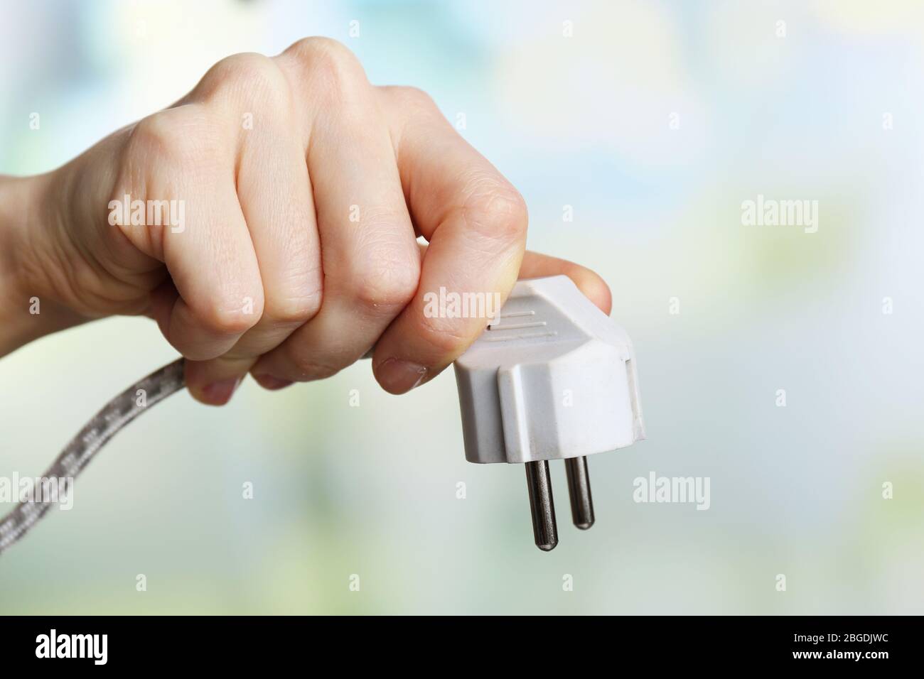 Hand holding electric plug on light background Stock Photo - Alamy
