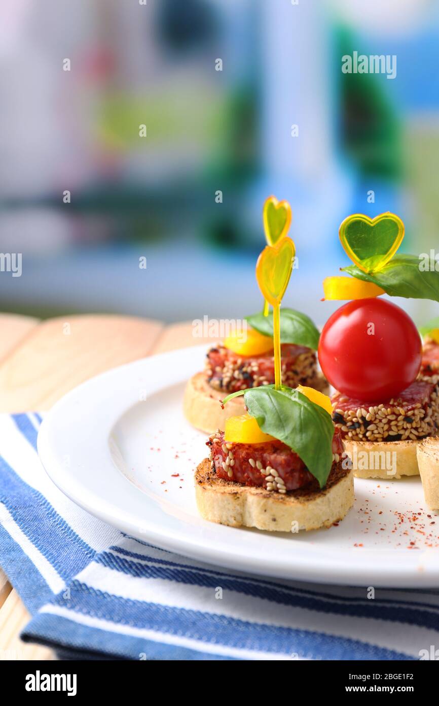 Tasty canapes with salami,tomato, pepper and basil leaves, on plate, on ...