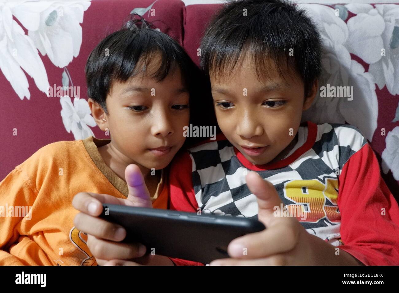 A boy plays a game in a smartphone while his brother is watching Stock ...
