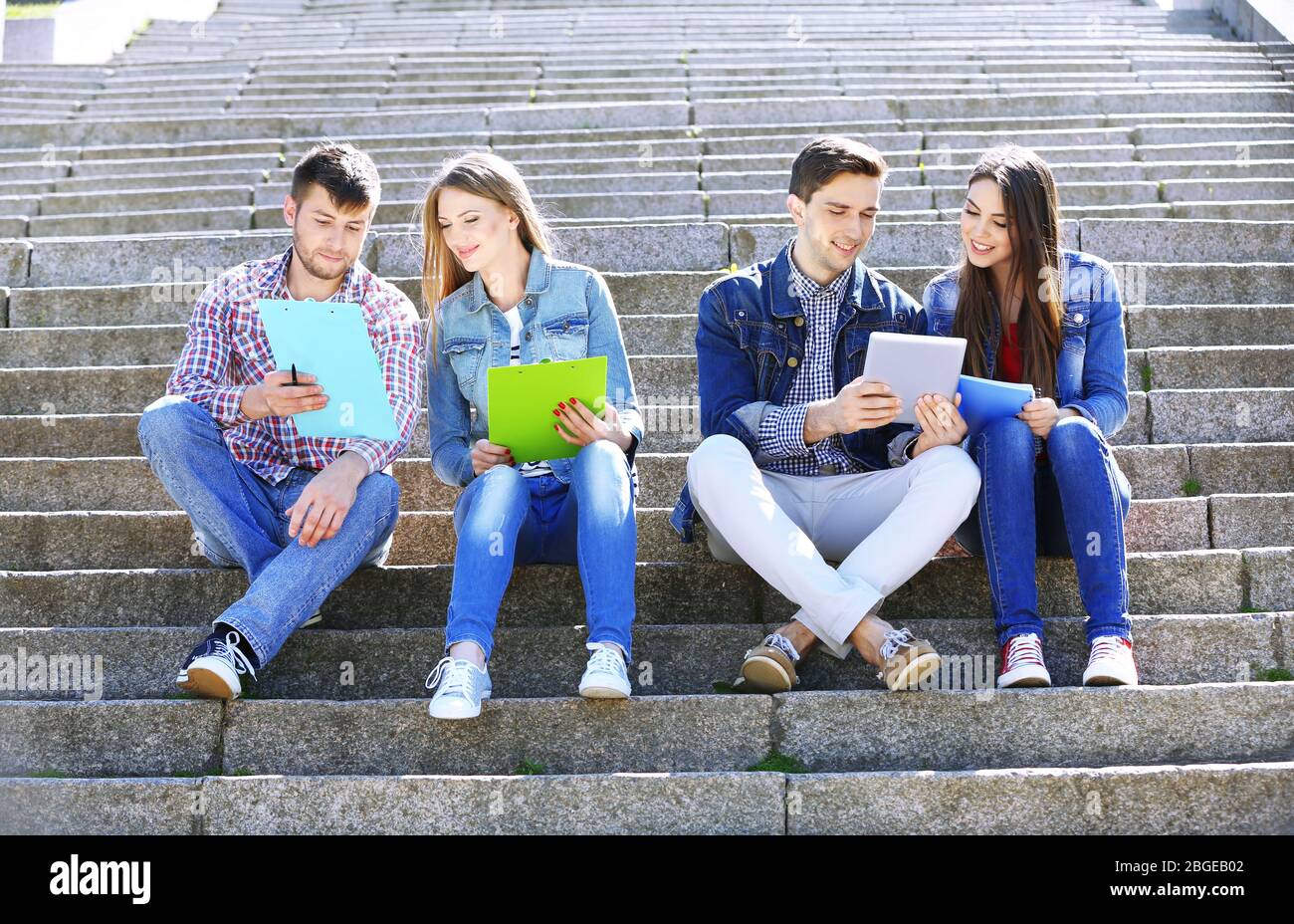 Happy students sitting on stairs in park Stock Photo - Alamy