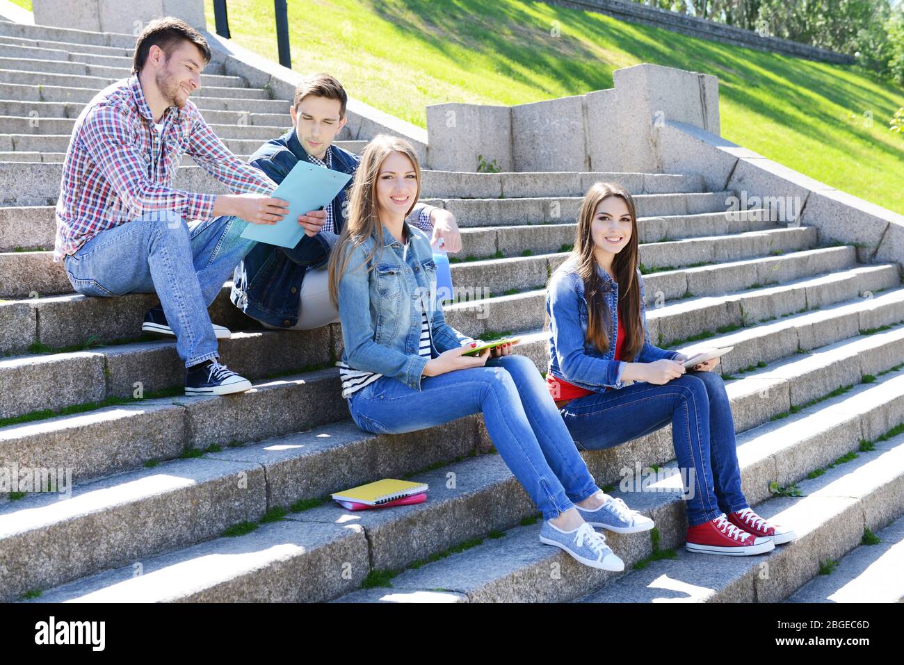 Happy students sitting on stairs in park Stock Photo - Alamy
