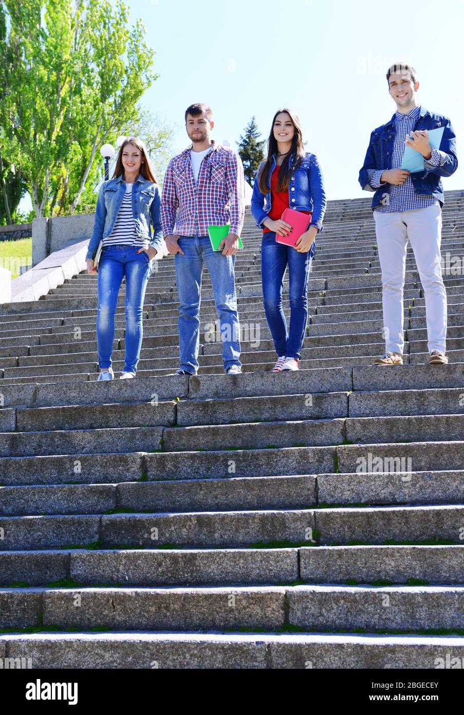 Happy students on stairs in park Stock Photo - Alamy
