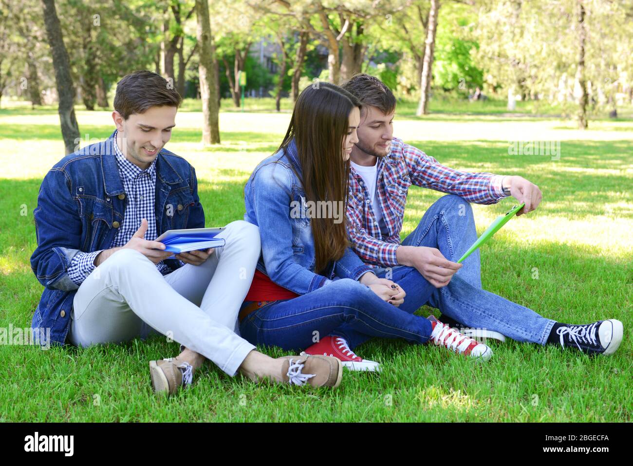 Happy students sitting in park Stock Photo - Alamy