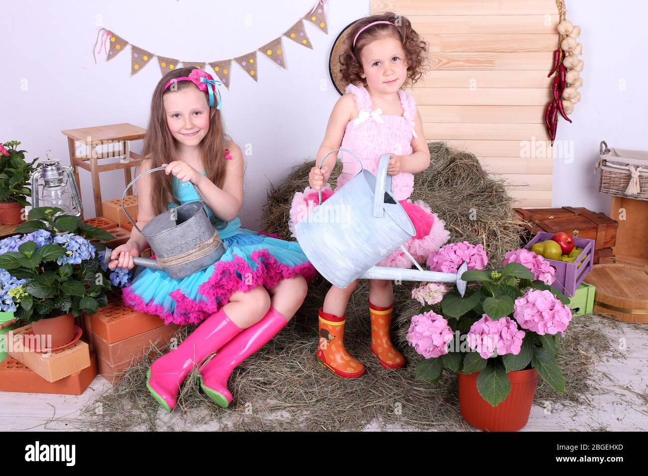 Beautiful small girls in petty skirts holding watering cans on country ...