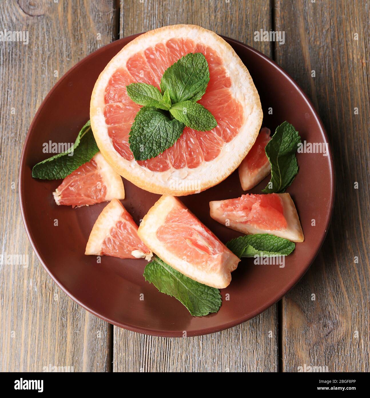 Ripe chopped grapefruit with mint leaves on plate, on wooden background ...