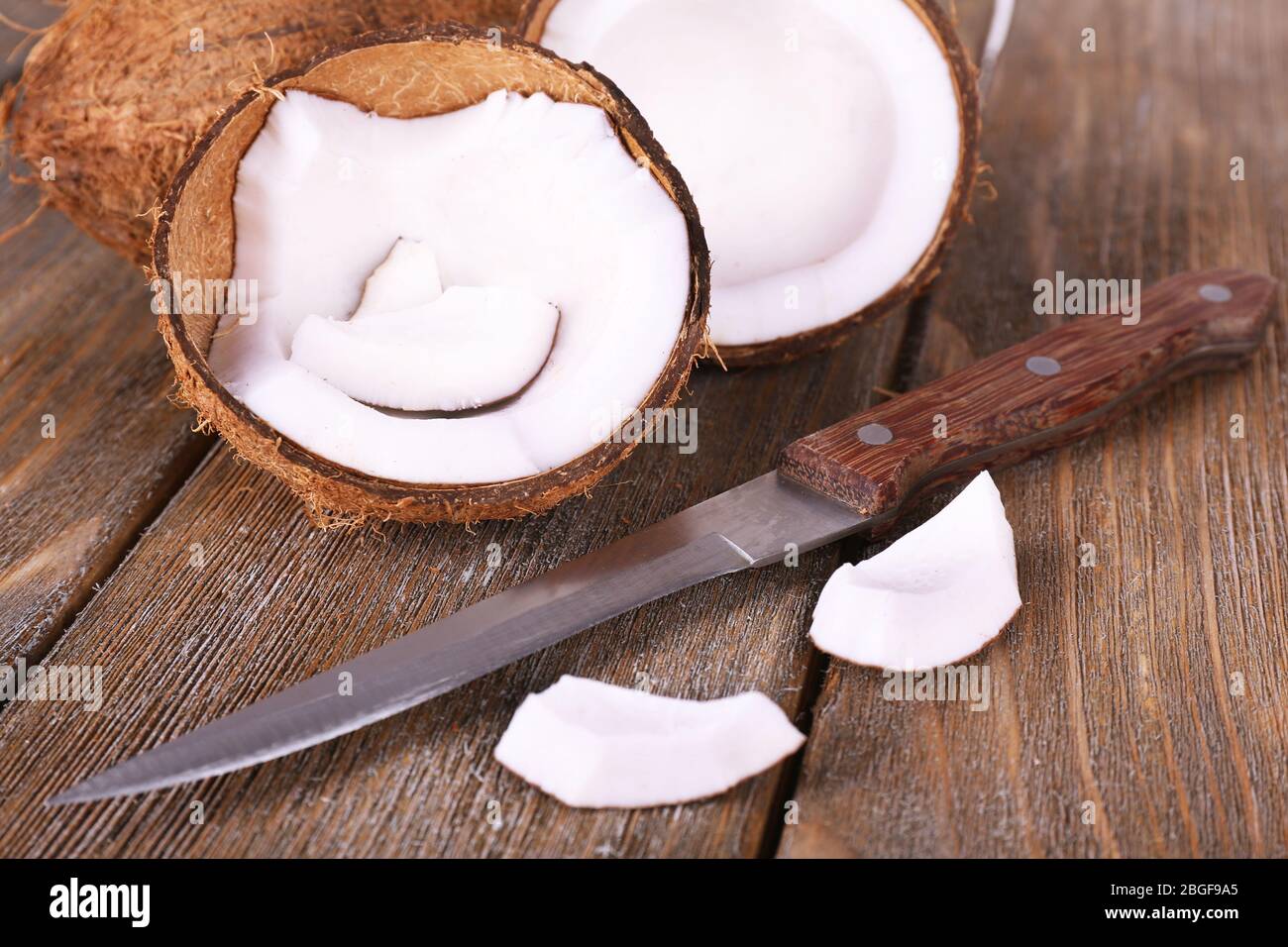 Broken coconut with knife on wooden background Stock Photo - Alamy