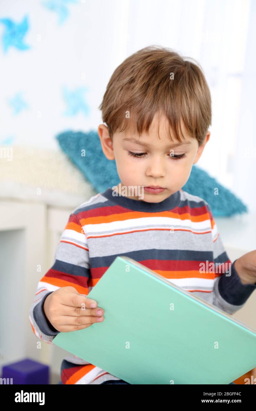 Cute little boy reading book in room Stock Photo - Alamy