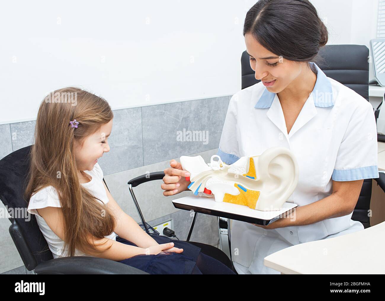 Audiologist showing a little girl an eardrum on model of human ear ...