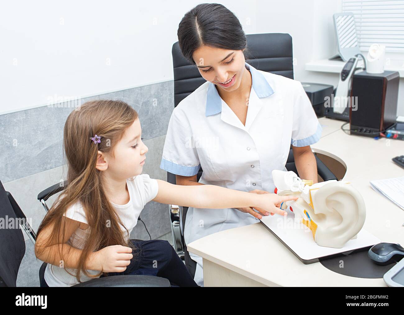 Audiologist showing a little girl an eardrum on model of human ear ...