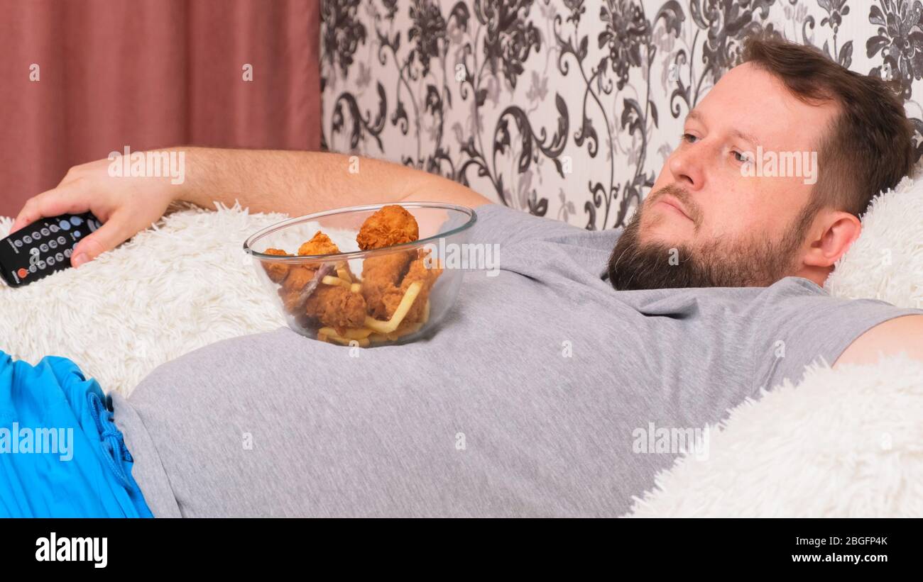 fat man with a big belly is lying on the couch with fast food and is ...