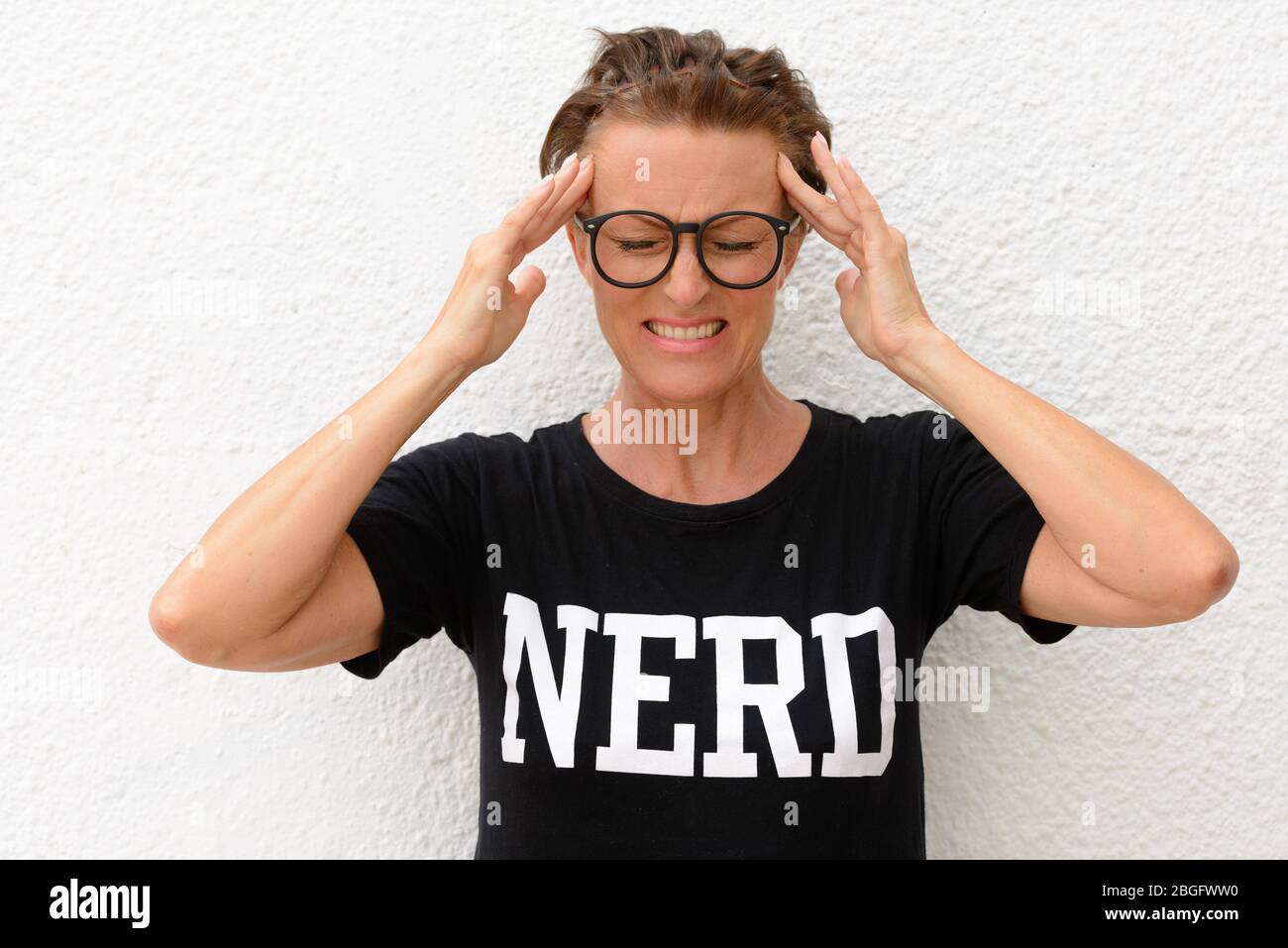 Stressed mature nerd woman having headache and standing against white ...