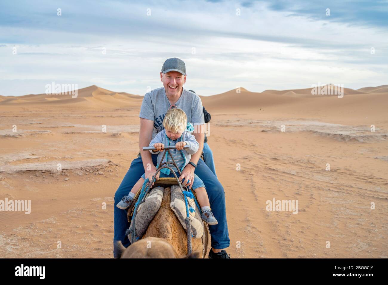Father and his two years old son riding a camel on sand of Sahara ...