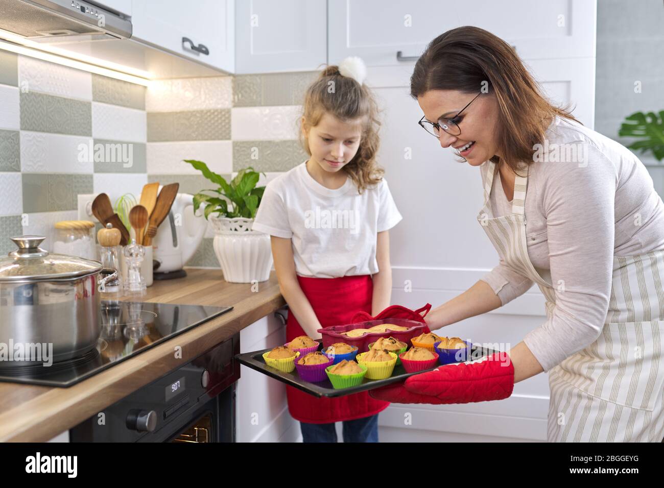 Mother in apron and daughter little helper preparing cupcakes together ...