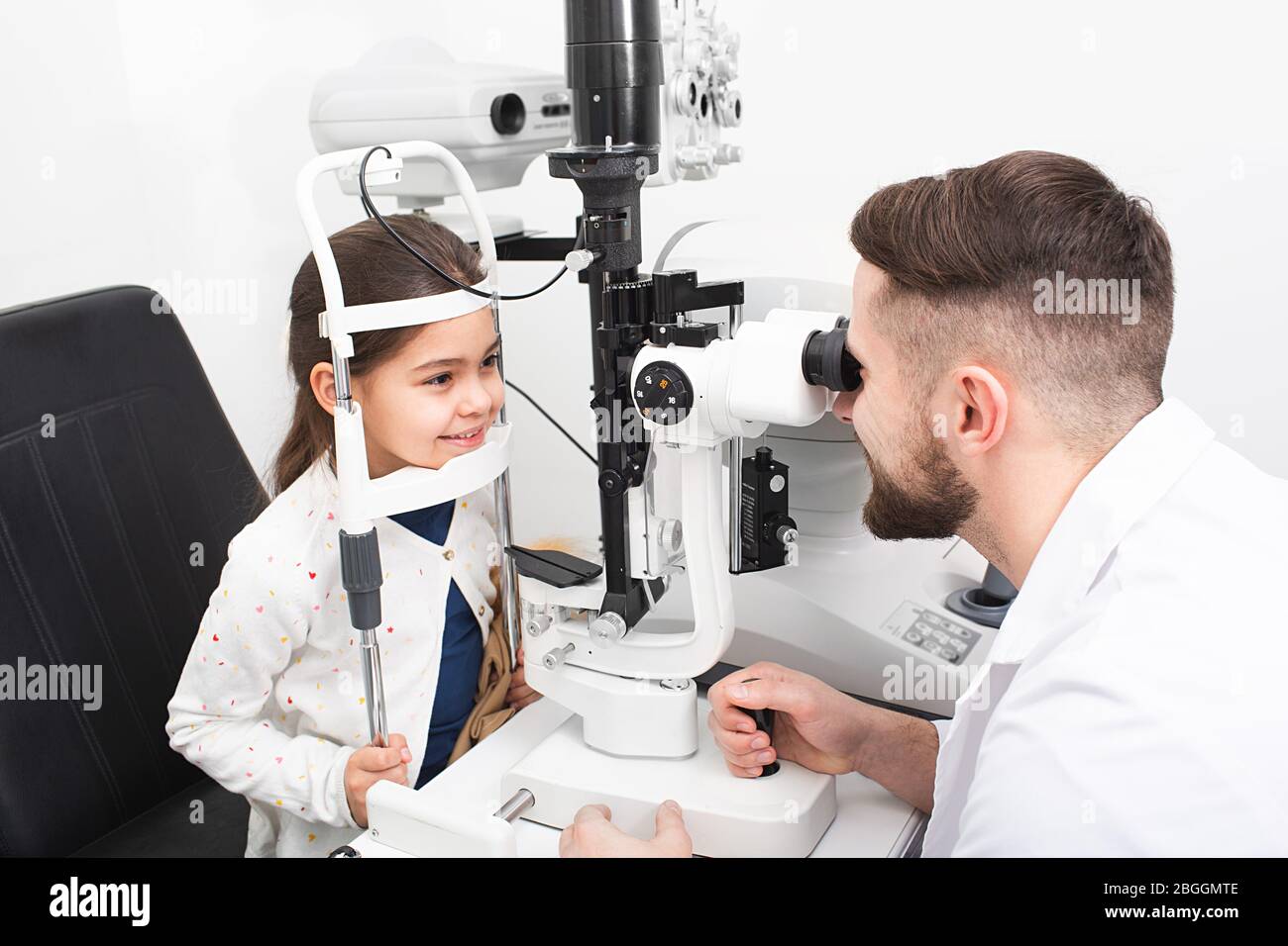 Optometrist doctor using a binocular slit-lamp examines the eye of a ...