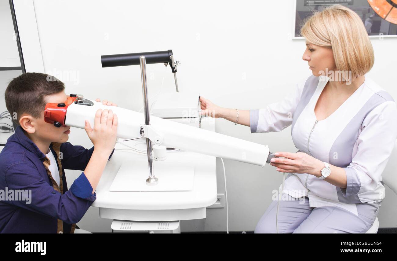 Boy looking into device to stimulate vision. Female ophthalmologist ...