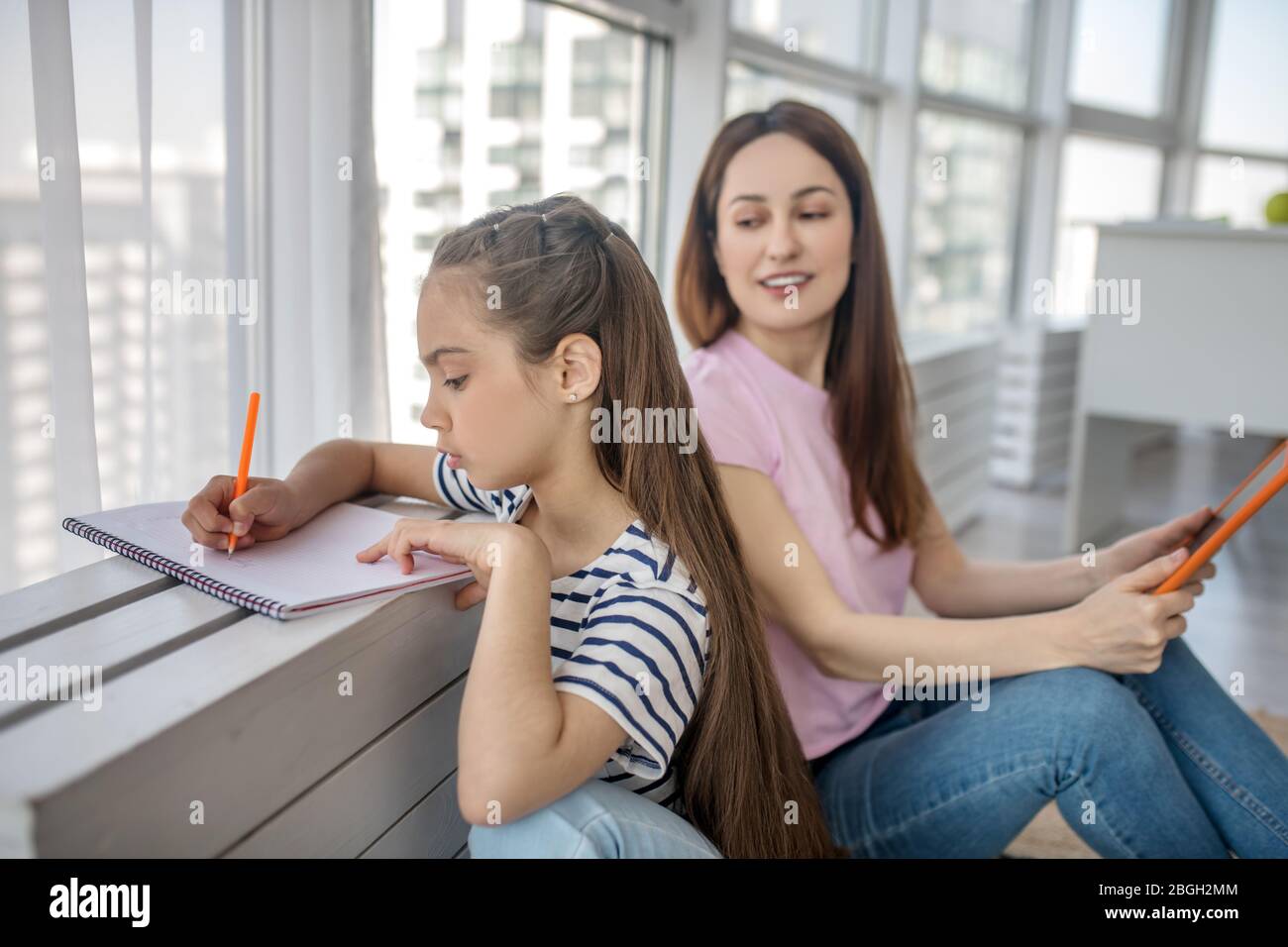 Mom with tablet and sad daughter writing in notebook Stock Photo - Alamy
