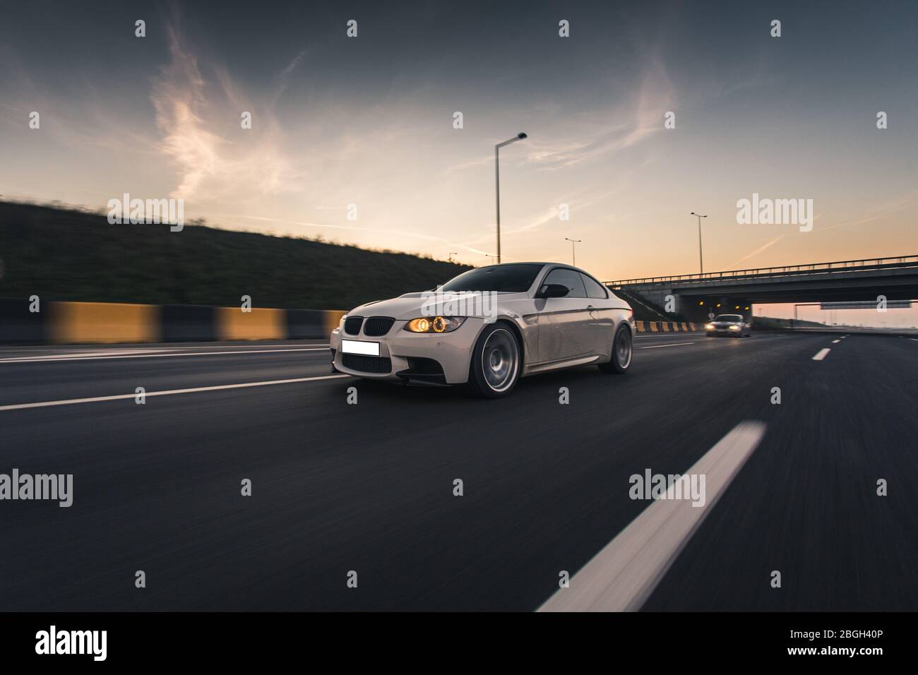 White sport car rush in the sunset time, front lights on, drive across ...