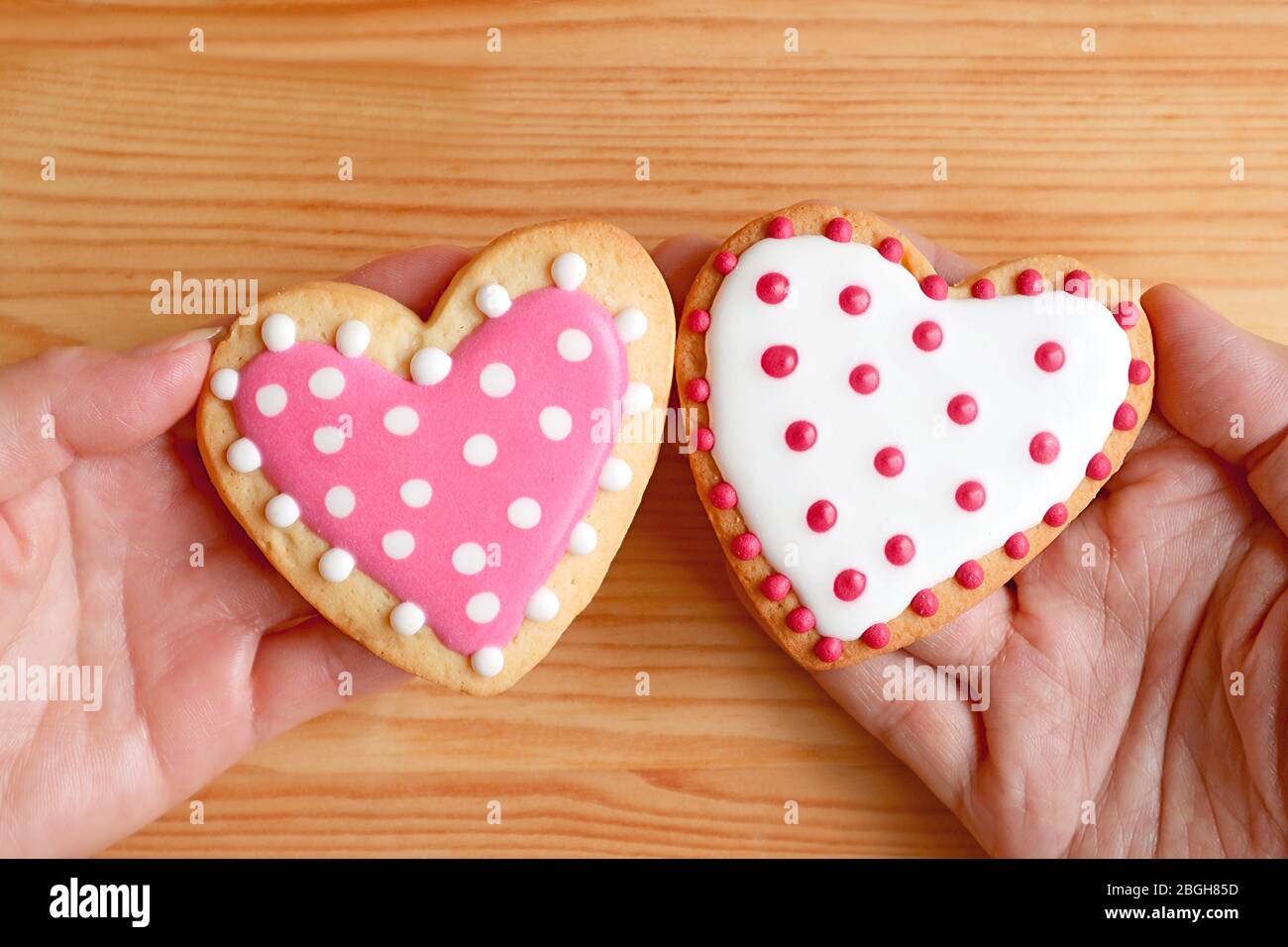 Pink and white dotted heart shaped cookies in couple's hands put ...