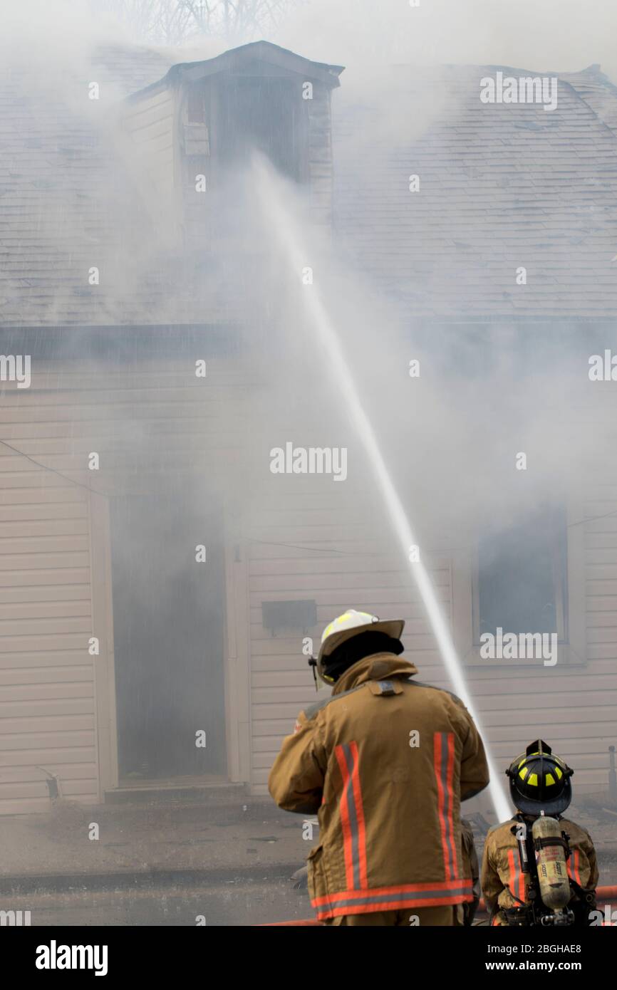 Fire men working at putting out house fire. Fire hose blasting water at ...
