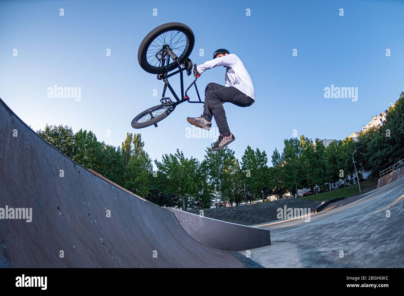 Biker jump high from quarter pipe ramp performing a tail whip trick ...