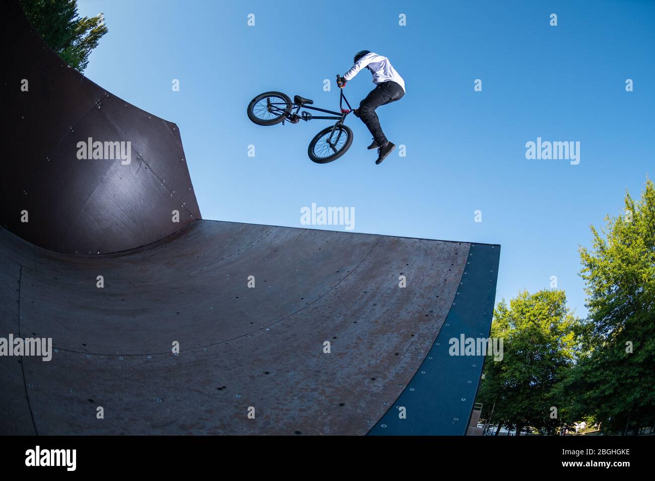 Biker jump high from quarter pipe ramp performing a tail whip trick ...