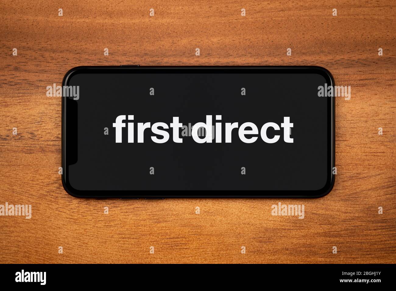 A smartphone showing the First Direct logo rests on a plain wooden ...