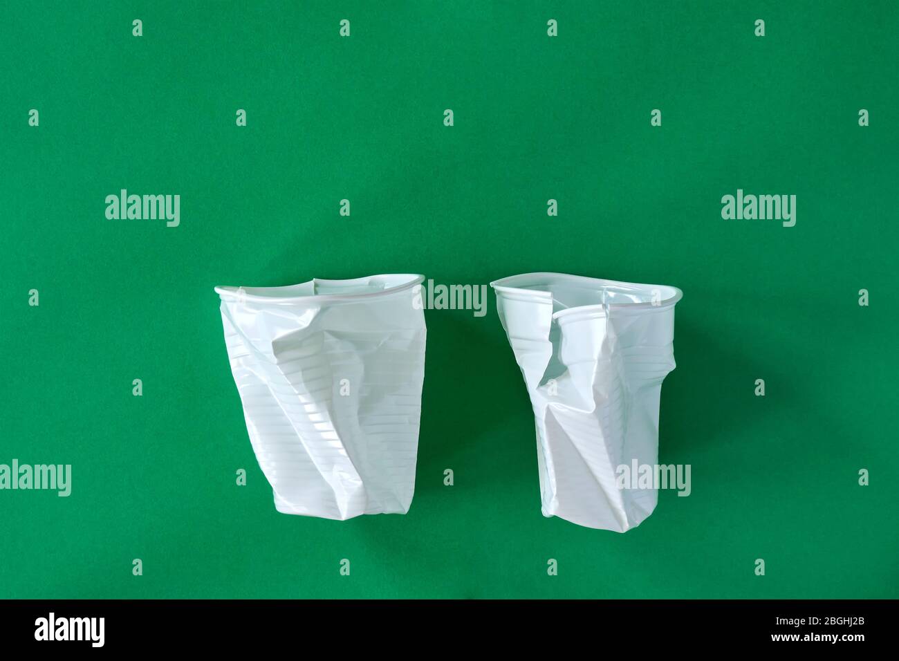 Two smashed white plastic coffee cups on a green background with copy ...