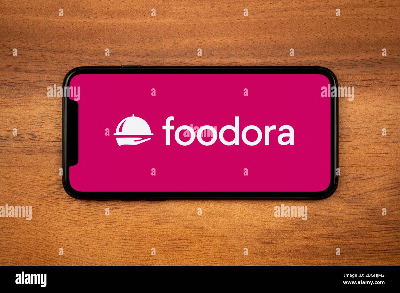 A smartphone showing the Foodora logo rests on a plain wooden table ...