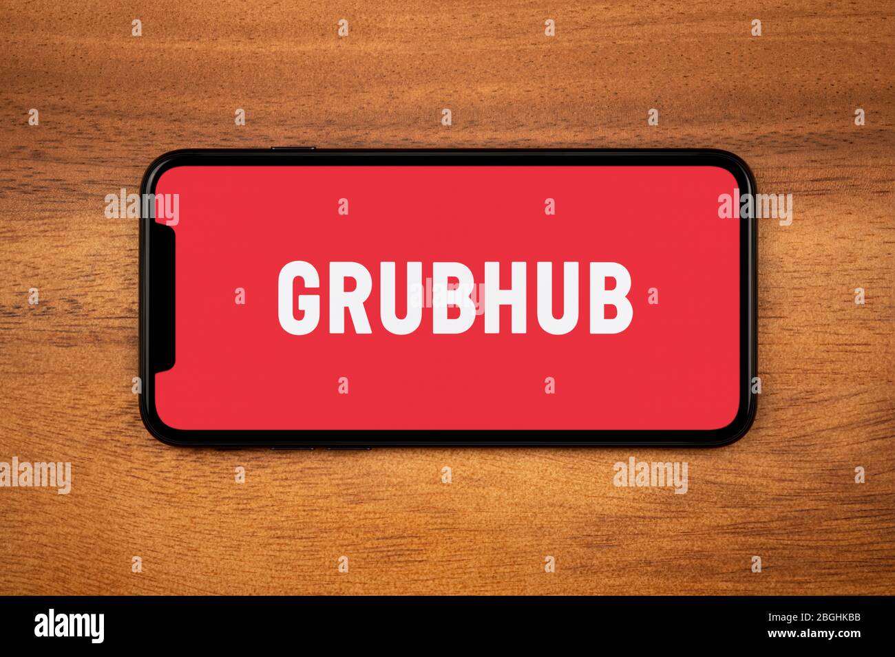 A smartphone showing the Grubhub logo rests on a plain wooden table ...