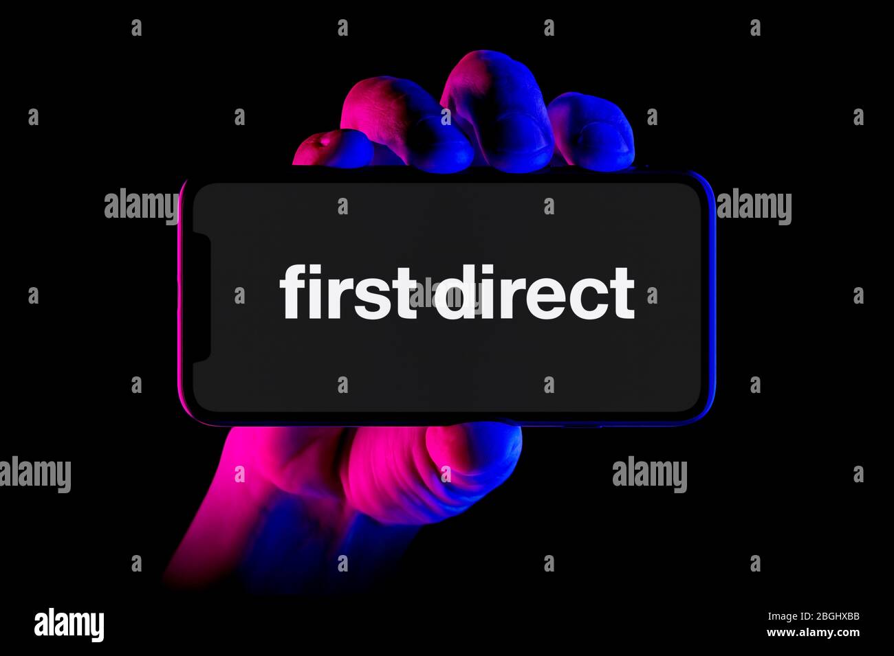 A smartphone displaying the First Direct logo is held by a hand shot on ...