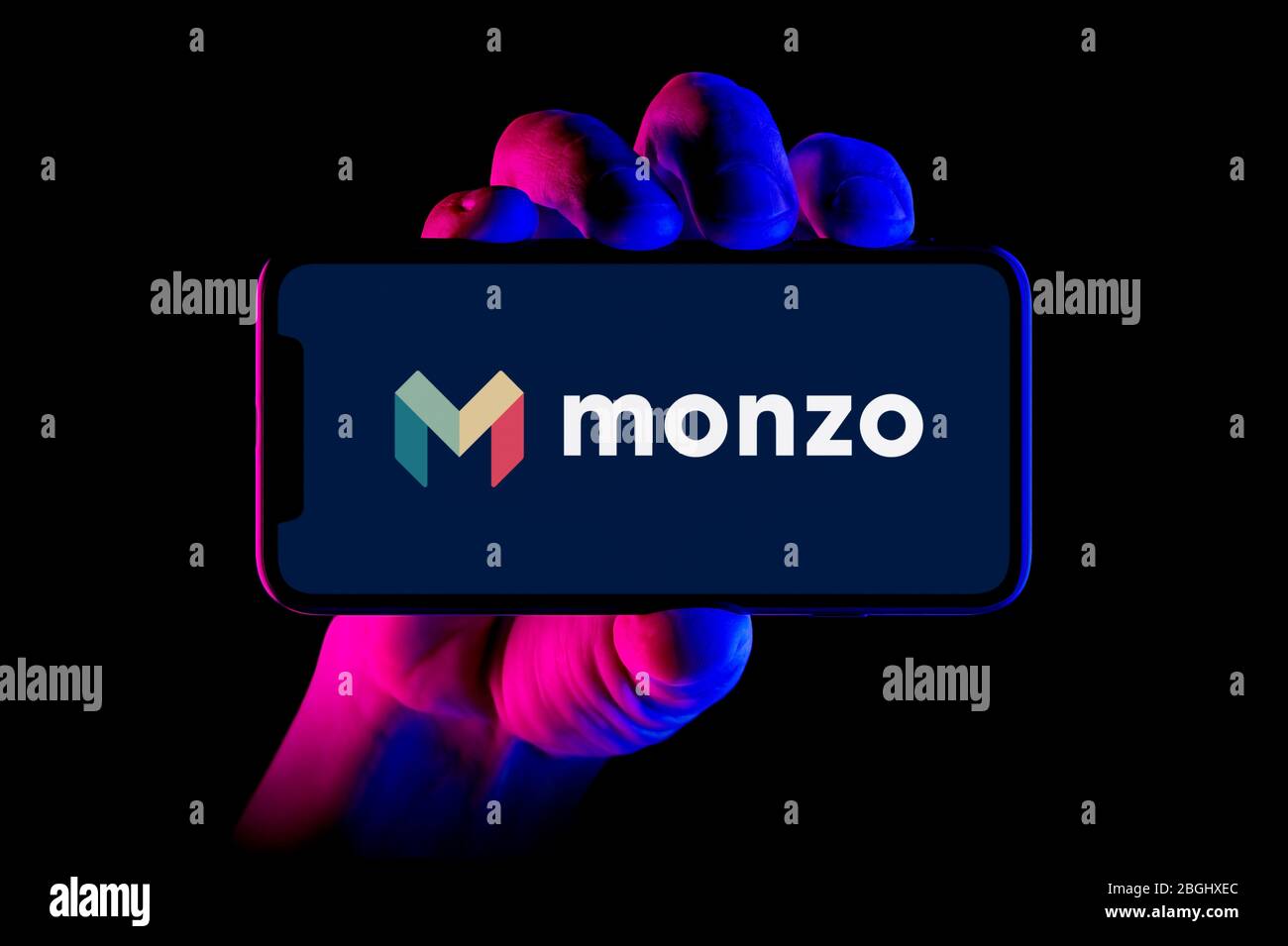 A smartphone displaying the Monzo Bank logo is held by a hand shot on a ...