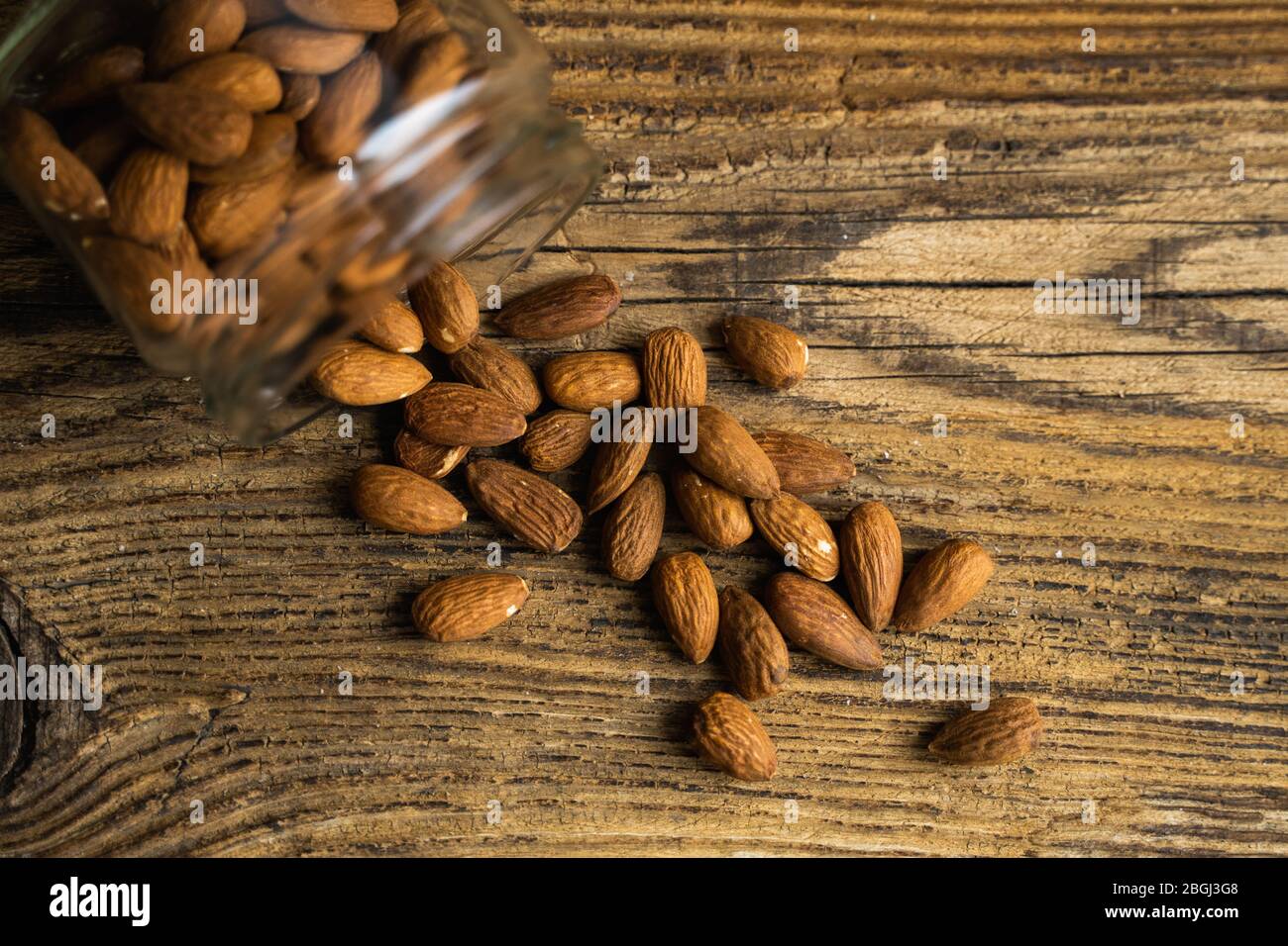 Almonds scattered on the wooden vintage table from a jar. Almond is a ...
