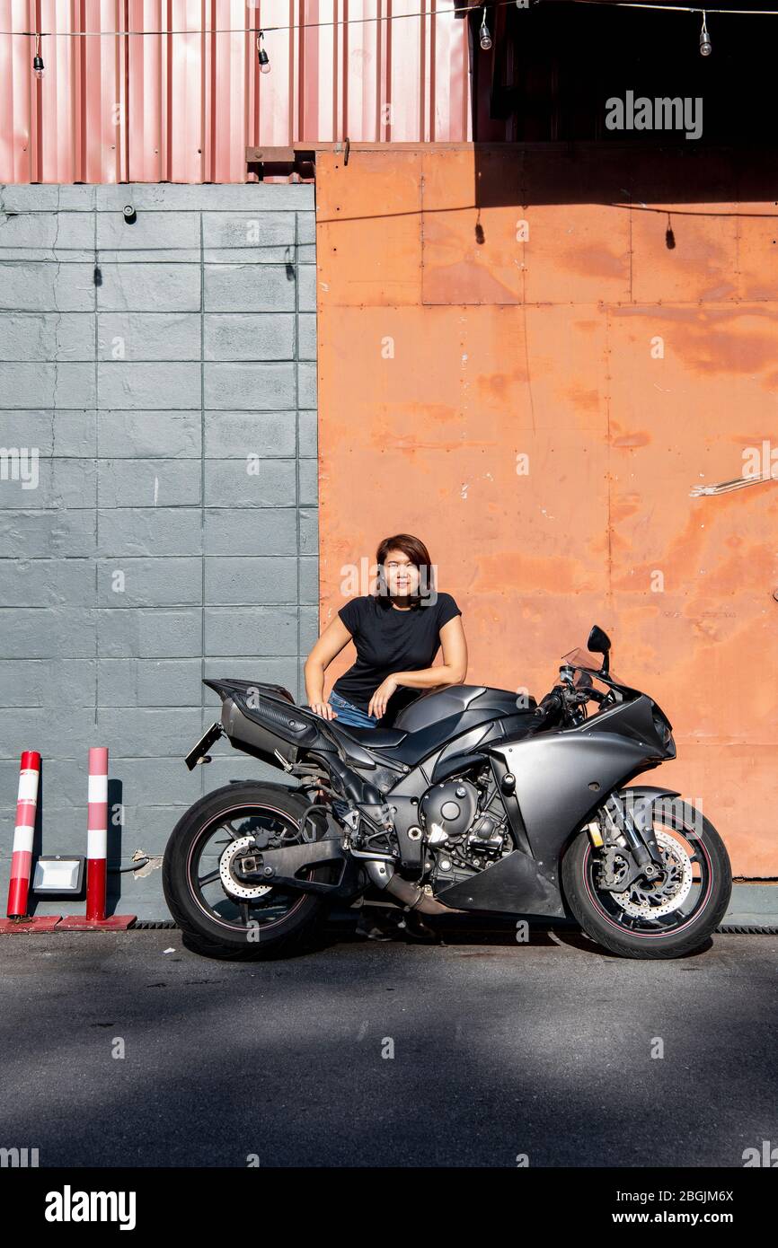 woman leaning on her motorcycle in front of warehouse in Bangkok Stock ...