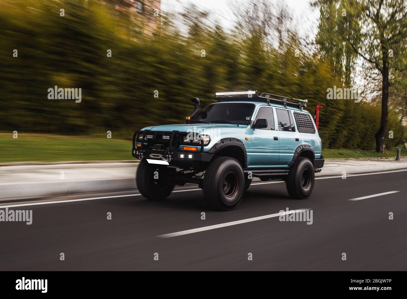 Blue offroader truck on the countryside highway across green trees ...